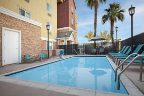 Uma piscina com espreguiçadeiras e uma área de estar coberta, cercada por um edifício com fachada de pedra e um canto vermelho.