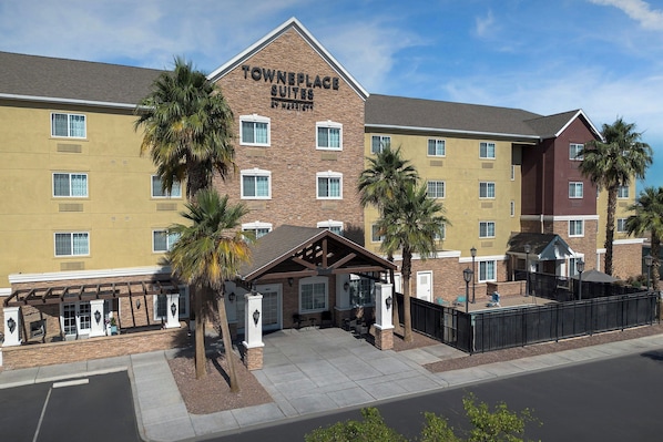 Um hotel com uma placa de destaque que diz "TOWNEPLACE SUITES BY MARRIOTT". Apresenta fachada de tijolos, várias janelas e uma área externa coberta com assentos.