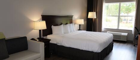 Quarto de hotel com uma cama grande, duas luminárias de cabeceira, um sofá e uma janela com cortinas.