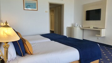 Quarto de hotel com uma cama, uma luminária, uma televisão e uma kitchenette compacta.