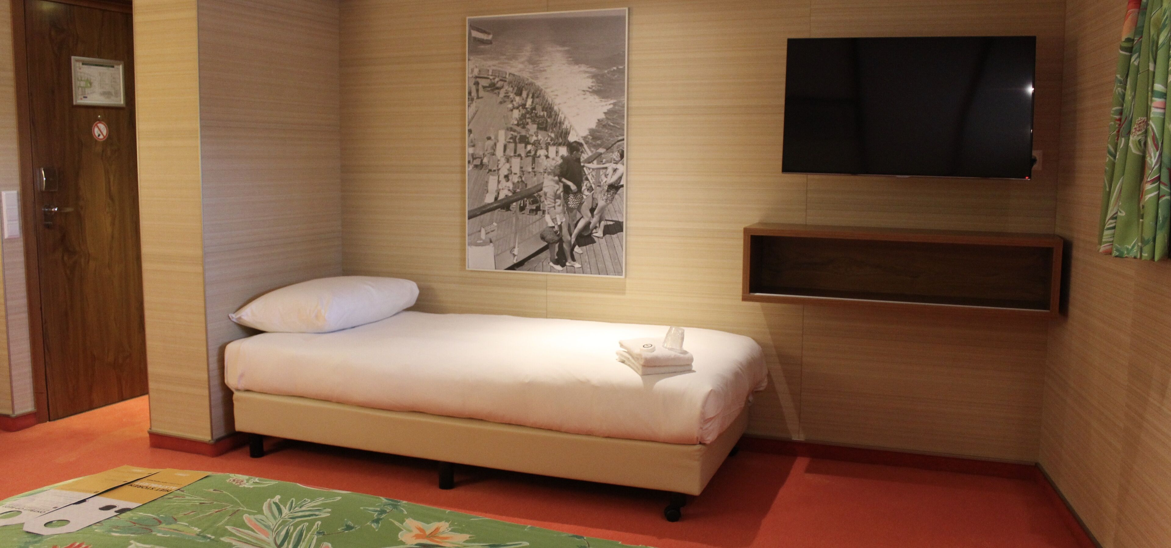 Quarto pequeno e bem arrumado com uma cama de casal, televisão montada e um quadro na parede.