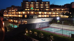 Um hotel com vários andares, quadra de tênis e área de estar externa.
