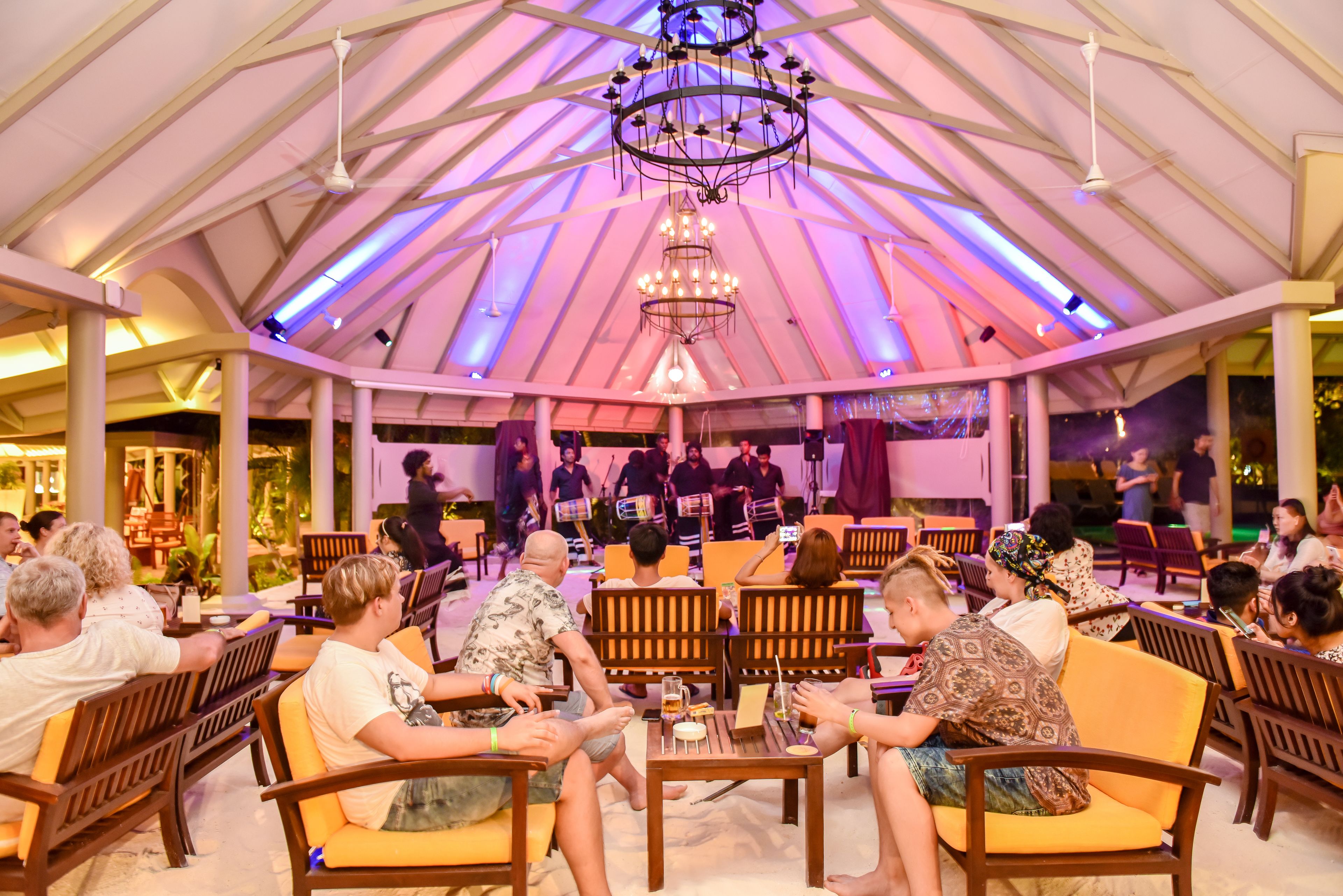 Uma grande estrutura em forma de tenda, com um candelabro, móveis de madeira e pessoas sentadas em mesas.