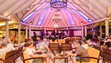 Uma grande estrutura em forma de tenda, com um candelabro, móveis de madeira e pessoas sentadas em mesas.