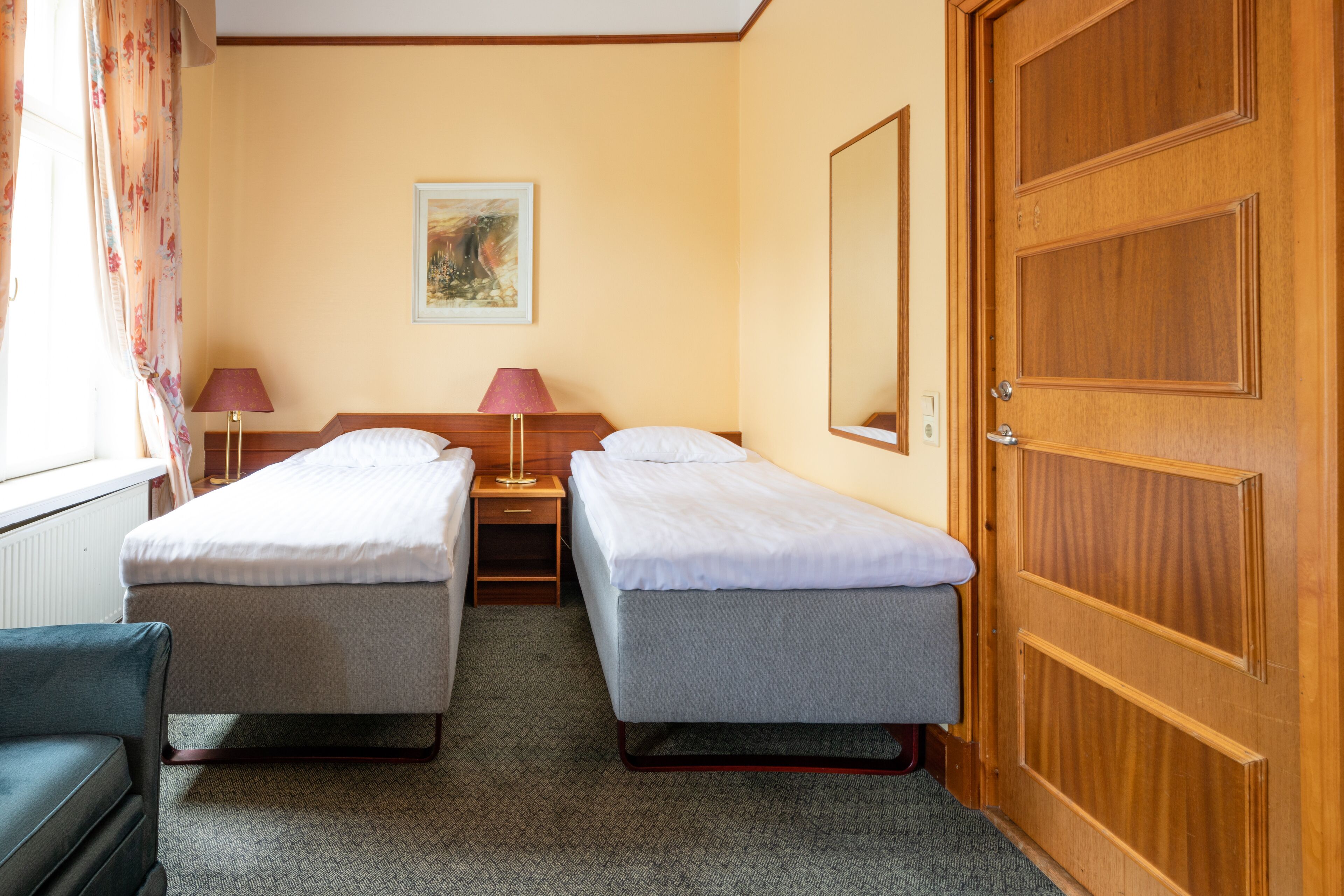 Quarto de hotel com duas camas de solteiro, uma porta de madeira e uma obra de arte emoldurada na parede.