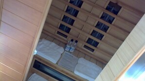 Quarto de hotel com teto de madeira, cama com lençóis brancos, uma mesa pequena com uma garrafa de água e um cardápio sobre a mesa.