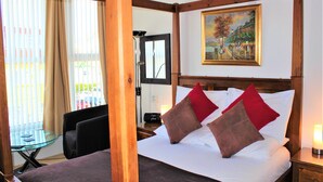 Quarto de hotel com uma cama grande, uma escrivaninha com cadeira, uma janela com cortinas e um quadro na parede.