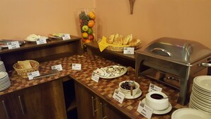 Buffet com alimentos identificados, incluindo queijos, presunto, abacate, frutas, pão, ovos e mel.