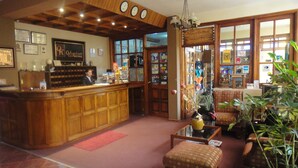Um saguão com balcão de atendimento em madeira, um candelabro, uma máquina de café e uma placa indicando