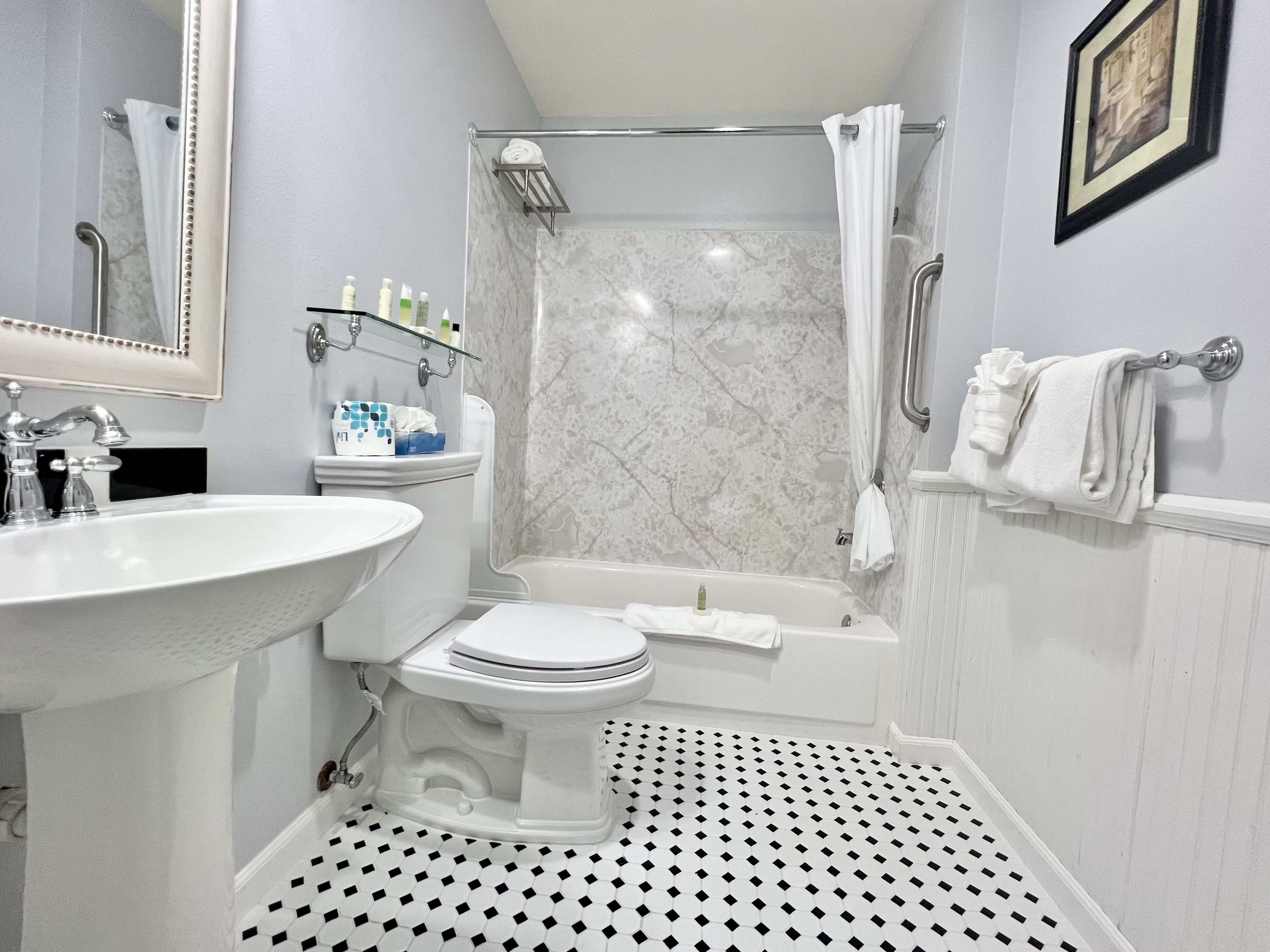 Casa de banho com lavatório branco, sanita e banheira, paredes de mármore e chão com padrão a preto e branco.