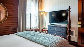 Quarto de hotel com uma cama grande, televisão, penteadeira e abajur.