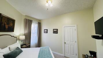 Quarto de hotel com cama, mesa de cabeceira, luminária, televisão e porta.
