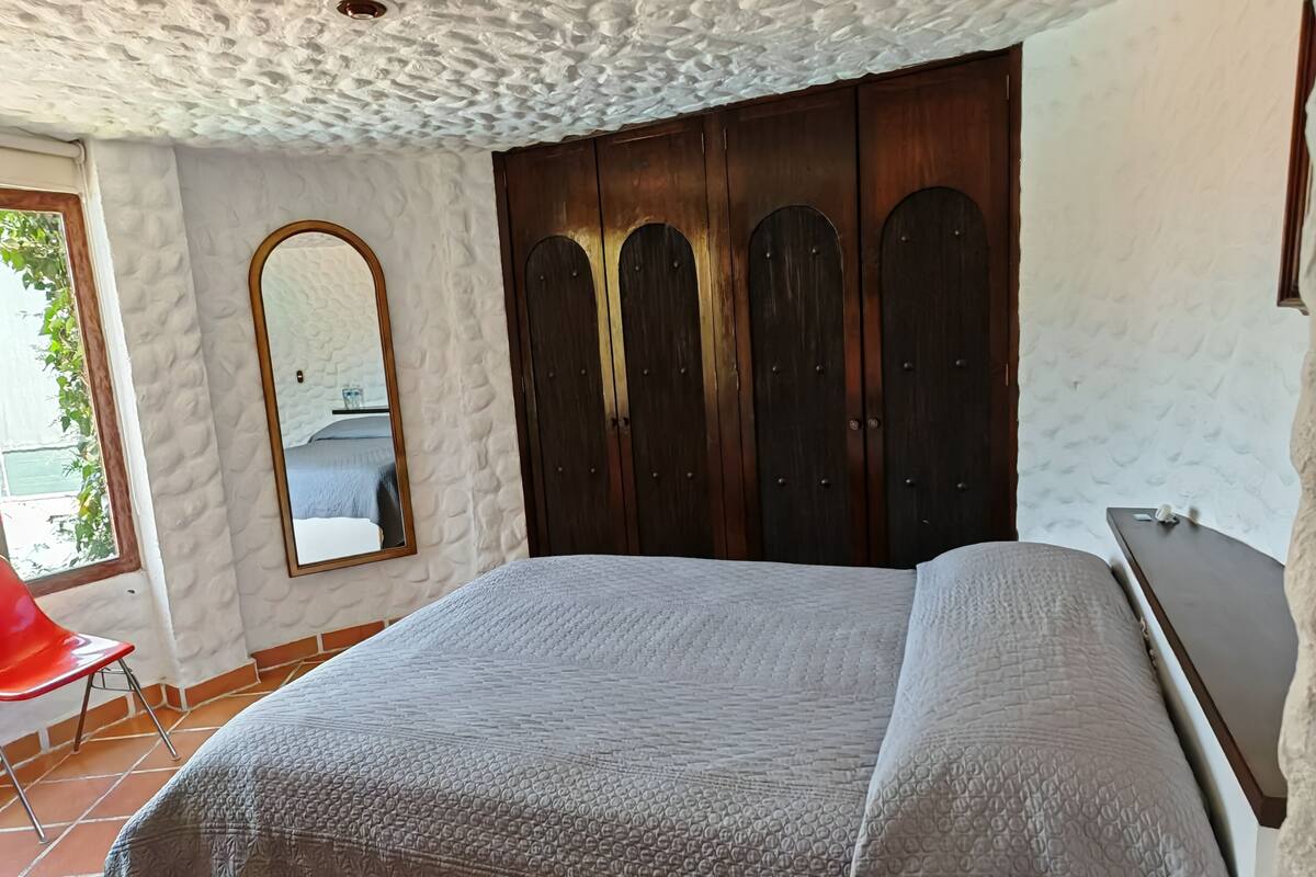 Quarto com uma cama grande, um guarda-roupa de madeira, um espelho e uma cadeira vermelha.