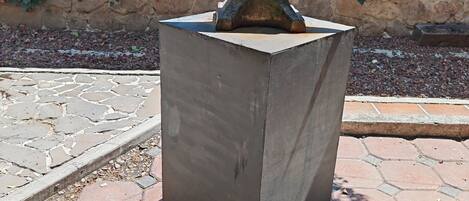 Escultura de bigorna de metal sobre um pedestal hexagonal em ambiente externo.
