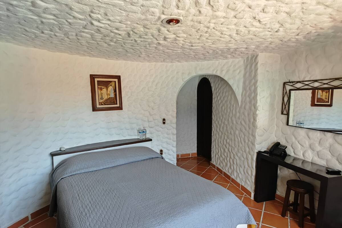 Quarto com cama, escrivaninha, cadeira e espelho.