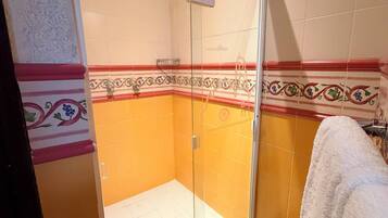 Um chuveiro com paredes de vidro, uma toalha branca pendurada na porta, paredes revestidas com uma borda decorativa e um ralo visível no chão.