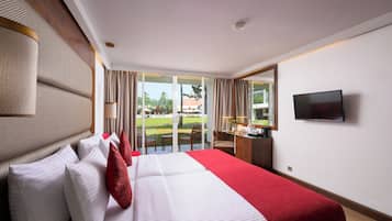 Quarto de hotel com cama, escrivaninha, televisão e vista para o exterior.