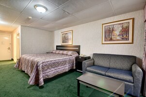 Quarto de hotel com cama, sofá, mesa de cabeceira e duas fotos emolduradas na parede.