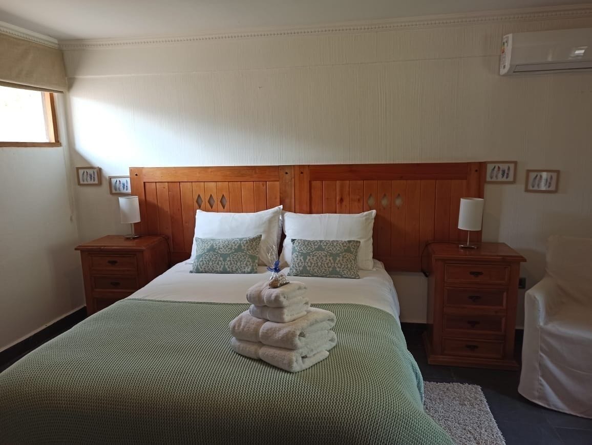 Uma cama bem arrumada com um edredom verde, duas mesas de cabeceira com luminárias e uma pilha de toalhas sobre a cama.