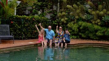 Uma família de quatro pessoas sentada à beira de uma piscina, cercada por vegetação exuberante.
