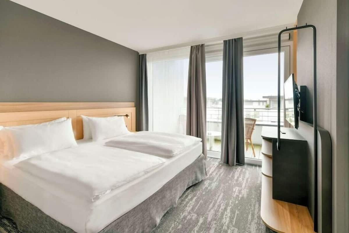 Quarto de hotel com cama grande, escrivaninha, cadeira, televisão e vista para o exterior.