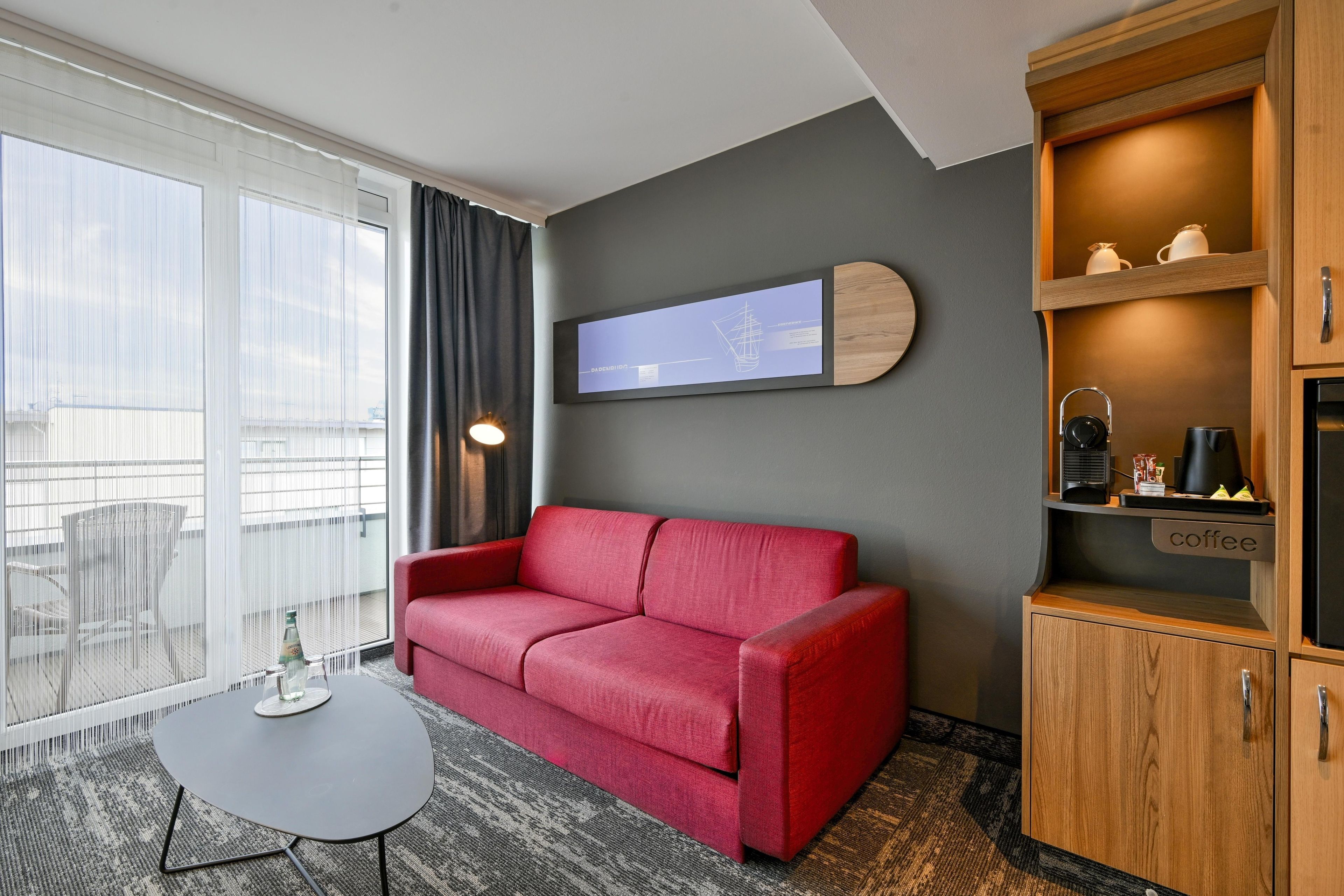 Quarto de hotel moderno com sofá vermelho, uma pequena mesa redonda e um espaço para café.