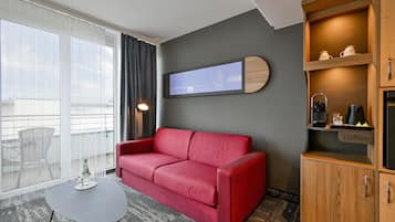 Quarto de hotel moderno com sofá vermelho, uma pequena mesa redonda e um espaço para café.