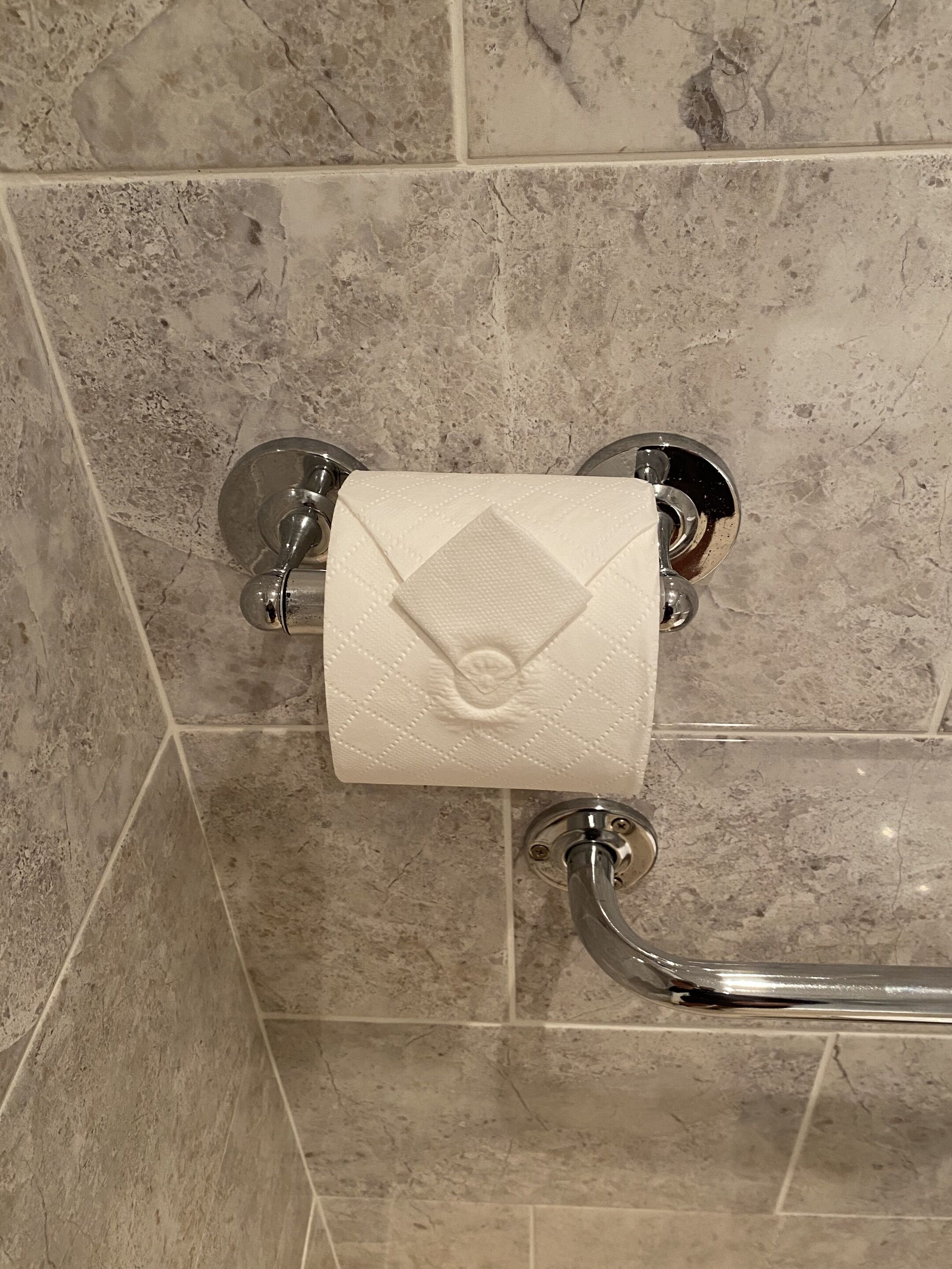 Um suporte de papel higiénico fixado numa parede revestida a azulejos em uma casa de banho.