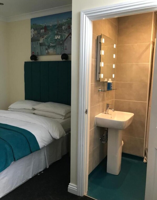 Quarto com cama, cabeceira verde-azulado e pintura de uma cidade costeira.