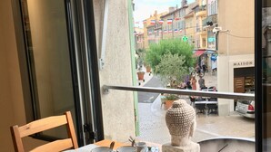 Uma área de refeições com uma mesa posta para dois, vista para a rua e um letreiro acima da janela com a inscrição "Löft".
