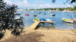Uma marina com barcos atracados, um cais de madeira e uma praia ao fundo.