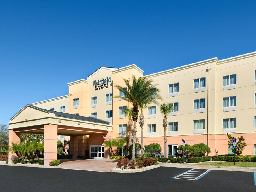 Um hotel Fairfield Inn & Suites com entrada coberta, palmeiras e estacionamento.