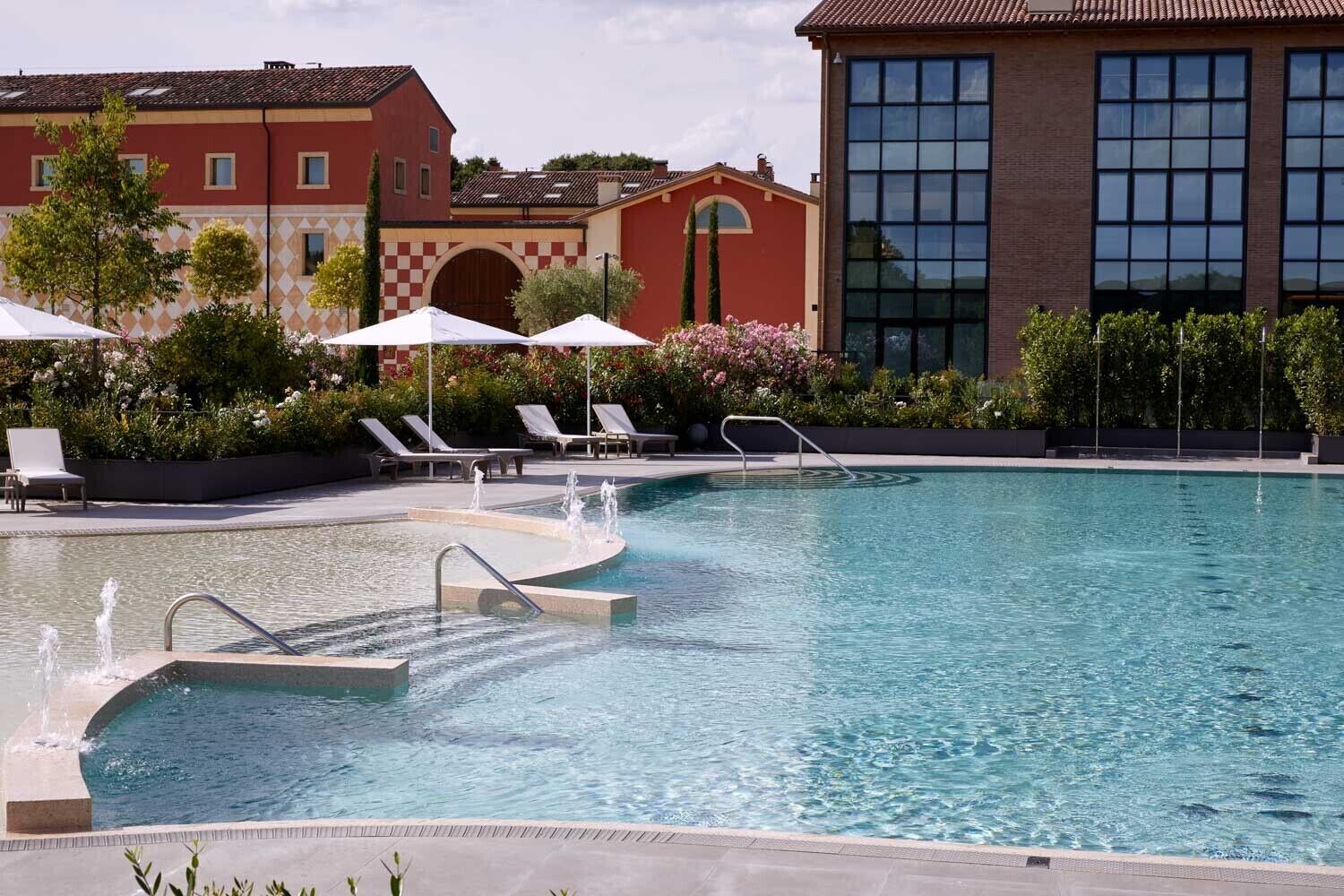 Piscina com espreguiçadeiras e guarda-sóis, rodeada por edifícios com diversos estilos arquitetônicos.