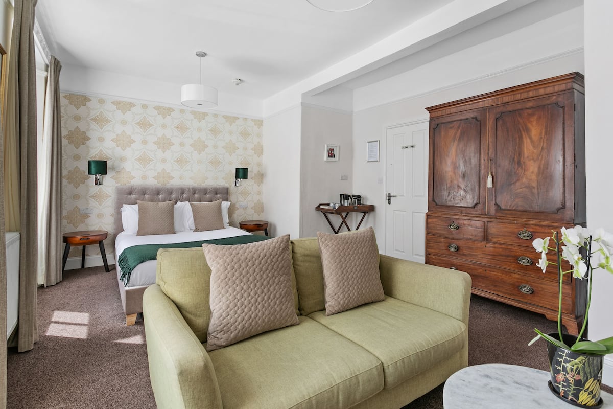 Quarto com cama, sofá verde, guarda-roupa de madeira e mesa de cabeceira com abajur.