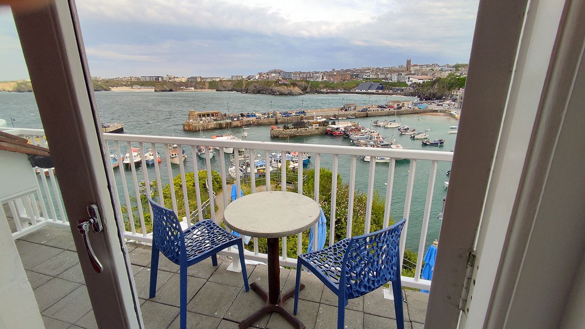 Varanda com mesa e cadeiras, vista para um porto com barcos e edifícios.