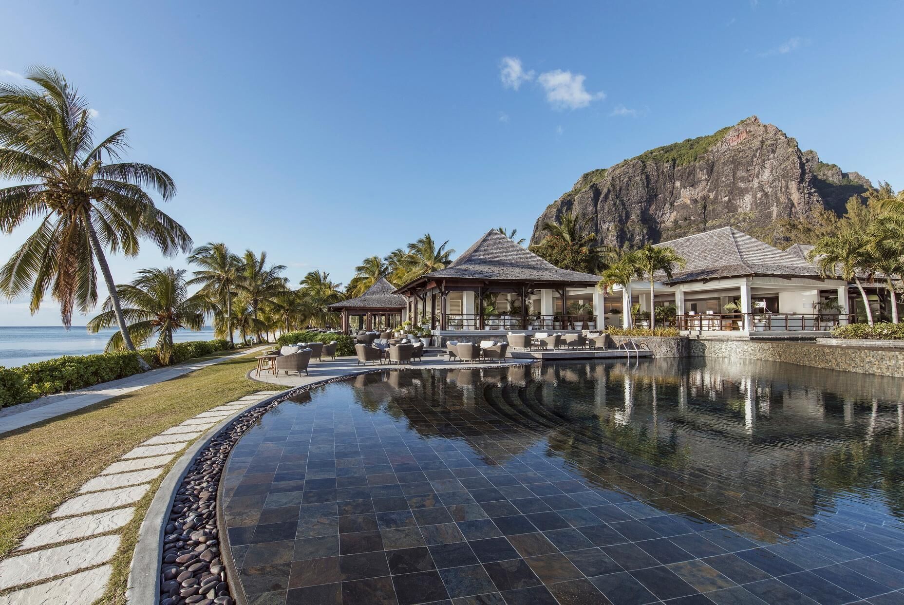 Um resort com piscina, áreas de descanso e vista para o oceano e uma montanha.