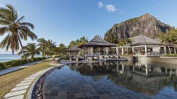 Um resort com piscina, áreas de descanso e vista para o oceano e uma montanha.