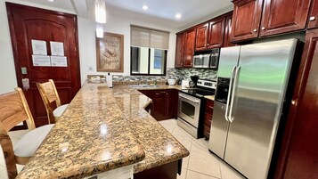 Uma cozinha com bancadas de granito, armários de madeira, eletrodomésticos de aço inoxidável e painel de azulejos.