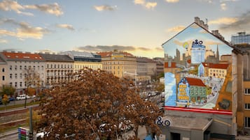 Paisagem urbana com um grande mural em um prédio, retratando diversas cenas e personagens urbanos.