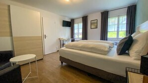 Quarto de hotel com cama, uma pequena mesa, televisão e janela com cortinas.