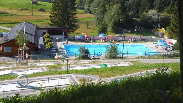 Área de piscina com uma piscina grande, um pequeno edifício e um parquinho.