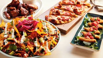 Diversos pratos, incluindo nachos, pizza e comidas fritas, sobre uma mesa.