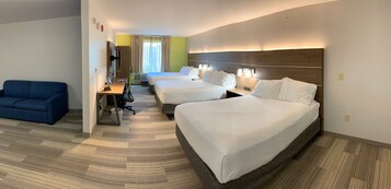 Quarto de hotel com duas camas, uma escrivaninha, uma cadeira e um sofá.