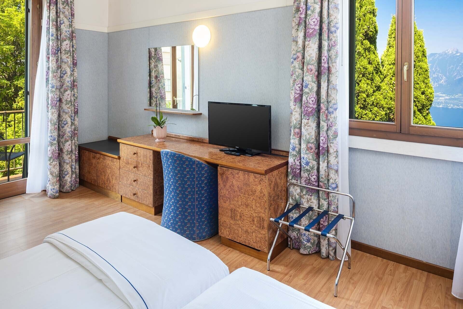 Um quarto com uma cama, uma escrivaninha com televisão, uma cadeira e uma janela com vista.
