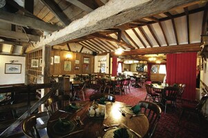 Um restaurante com vigas de madeira, várias mesas e cadeiras.