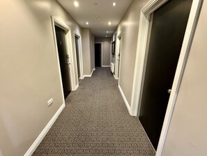Um corredor com carpete estampado, paredes brancas e portas que dão para os quartos.