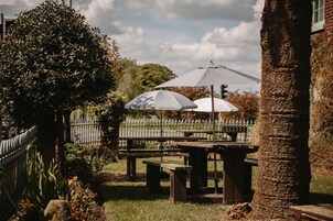 Um jardim com mesas de piquenique e guarda-sóis, cercado por uma vedação e árvores.