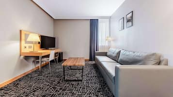 Quarto de hotel com sofá, televisão, escrivaninha e carpete estampado.