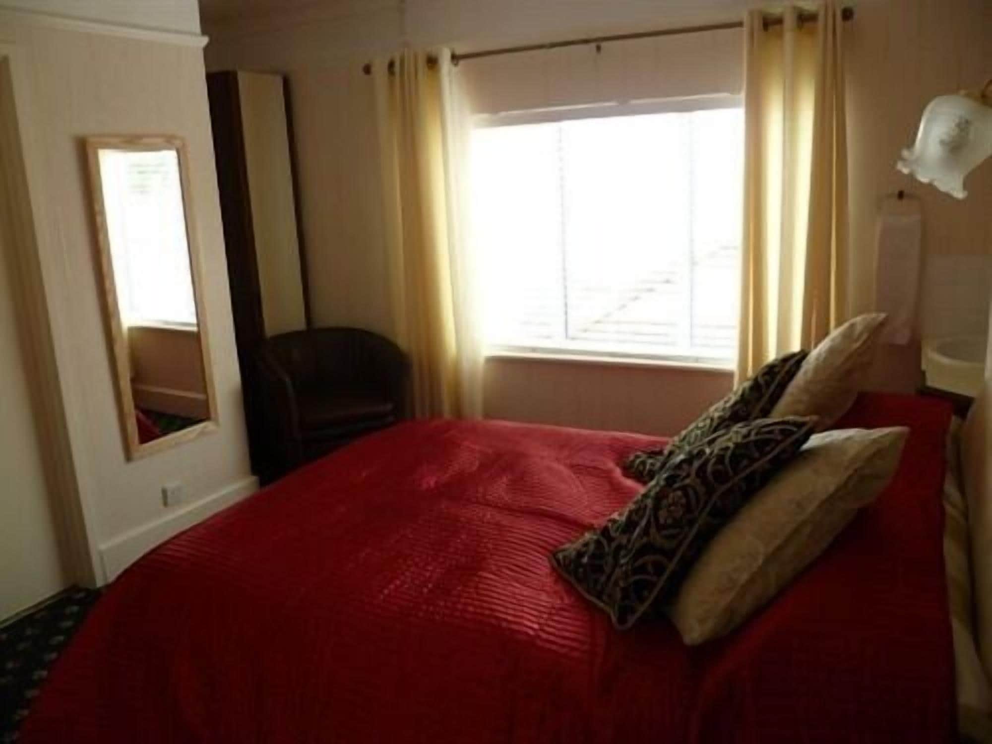 Quarto de hotel com cama, uma cadeira, janela com cortinas e um espelho.