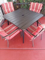 Um pátio com uma mesa de madeira escura e cadeiras listradas em vermelho e branco.